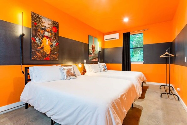 Quarto de hotel com duas camas, paredes laranja e obras de arte nas paredes.