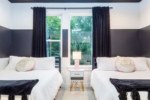 Quarto com duas camas, mesa de cabeceira, abajur e janela com cortinas.