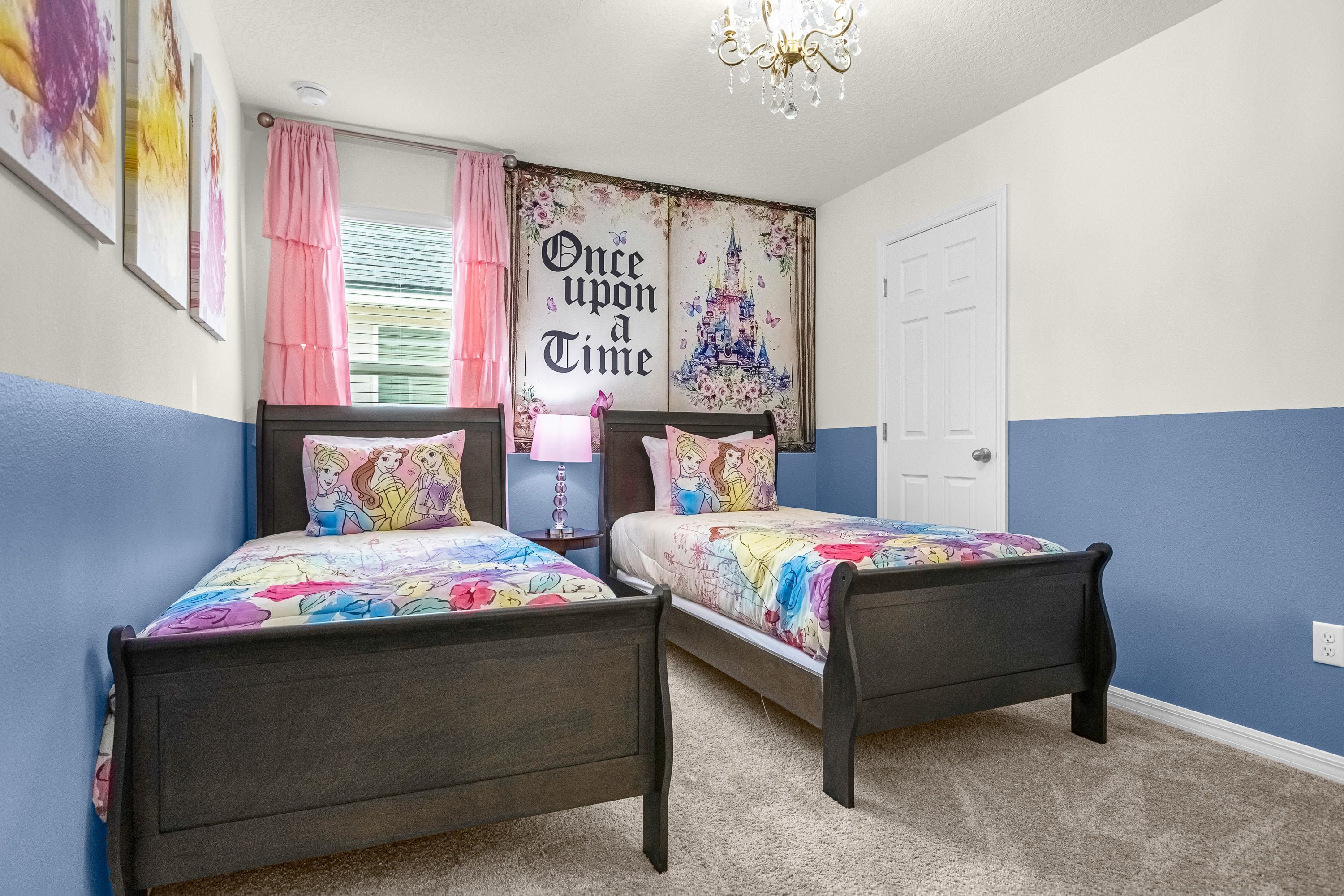 Quarto com duas camas, um candelabro, uma janela com cortinas cor-de-rosa e um pôster na parede.