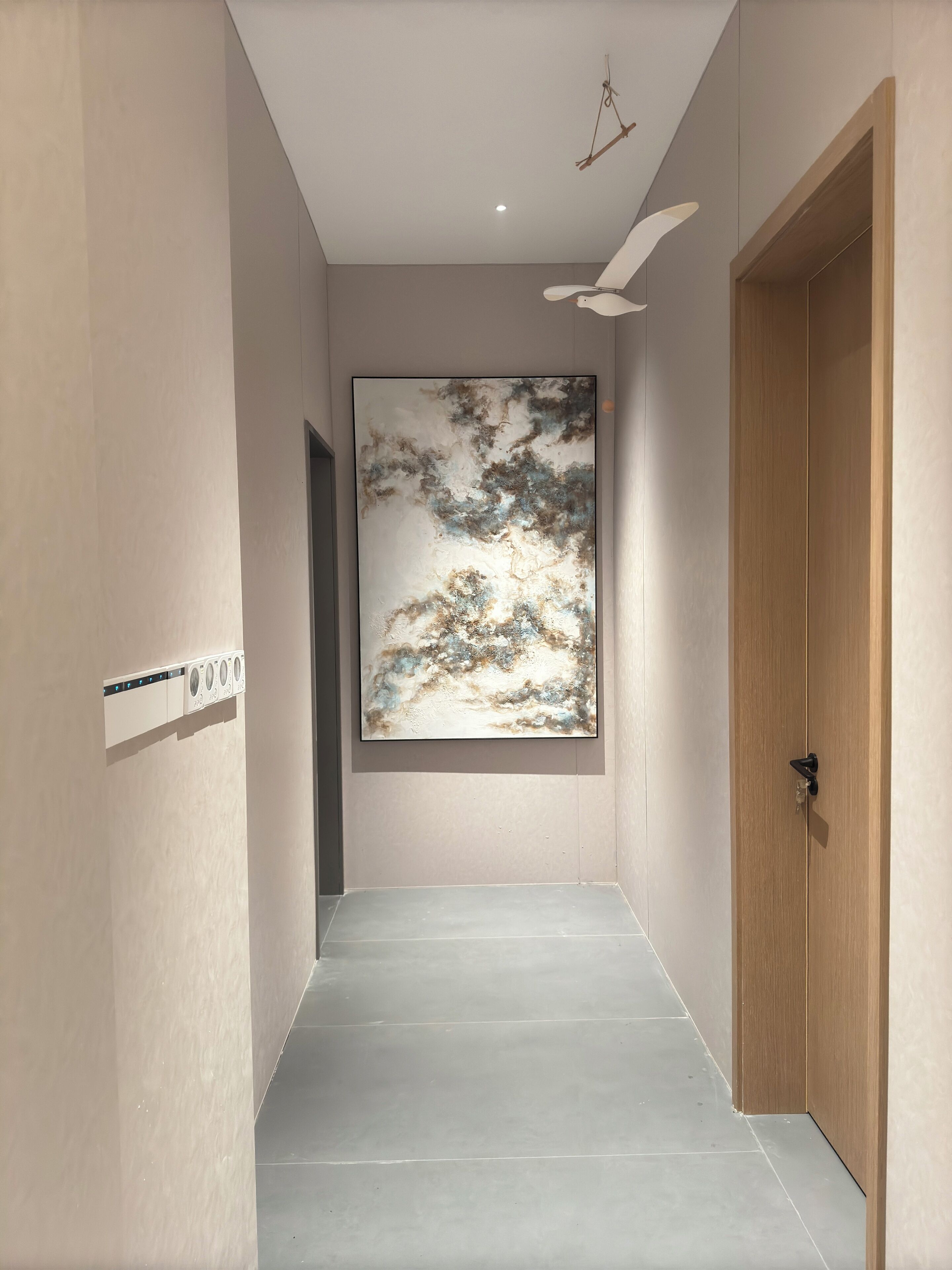 Um corredor com um lustre moderno, uma porta de madeira e uma grande pintura abstrata na parede.