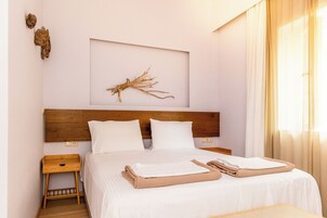 Uma cama bem arrumada com lençóis brancos, uma cabeceira de madeira e uma decoração de galho fixada na parede.