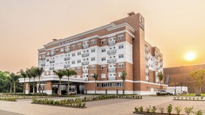 Hotel de vários andares com design moderno, apresentando varandas em cada andar, fachada de tijolos e área de entrada ajardinada.