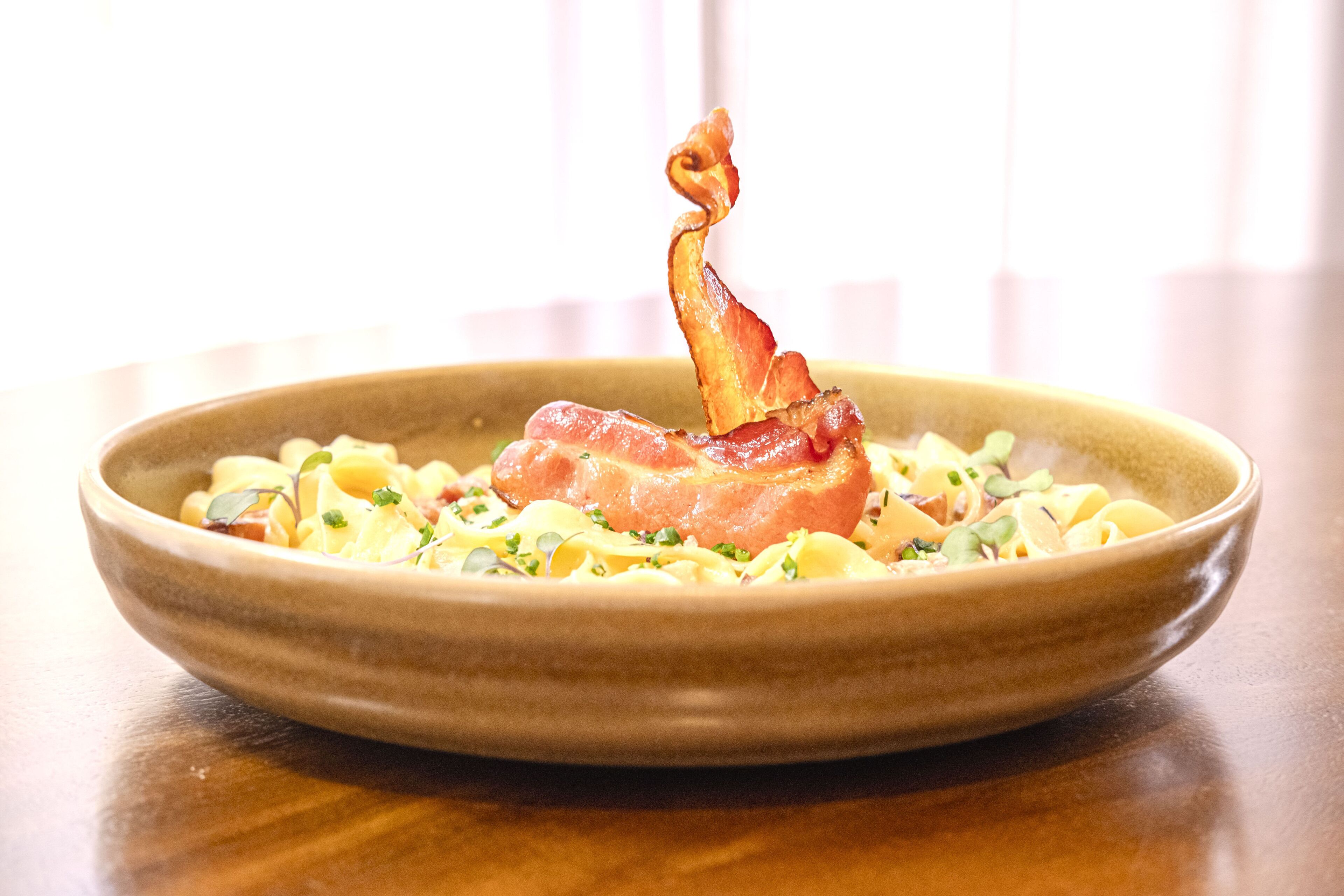 Uma tigela de massa com guarnição de bacon.