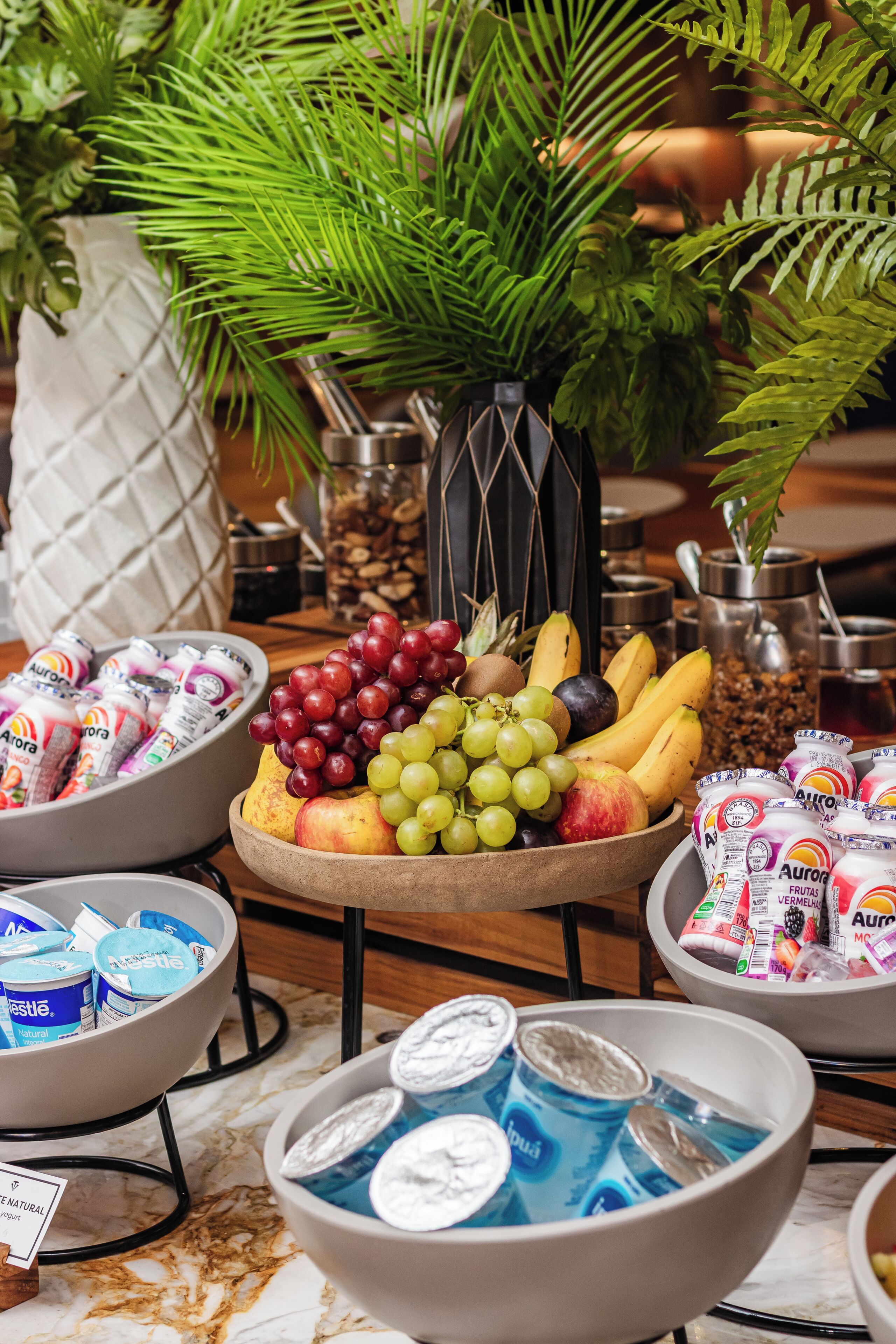 Uma mesa de buffet com diversas frutas, iogurte e bebidas enlatadas.