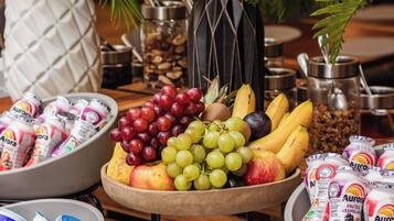 Uma mesa de buffet com diversas frutas, iogurte e bebidas enlatadas.