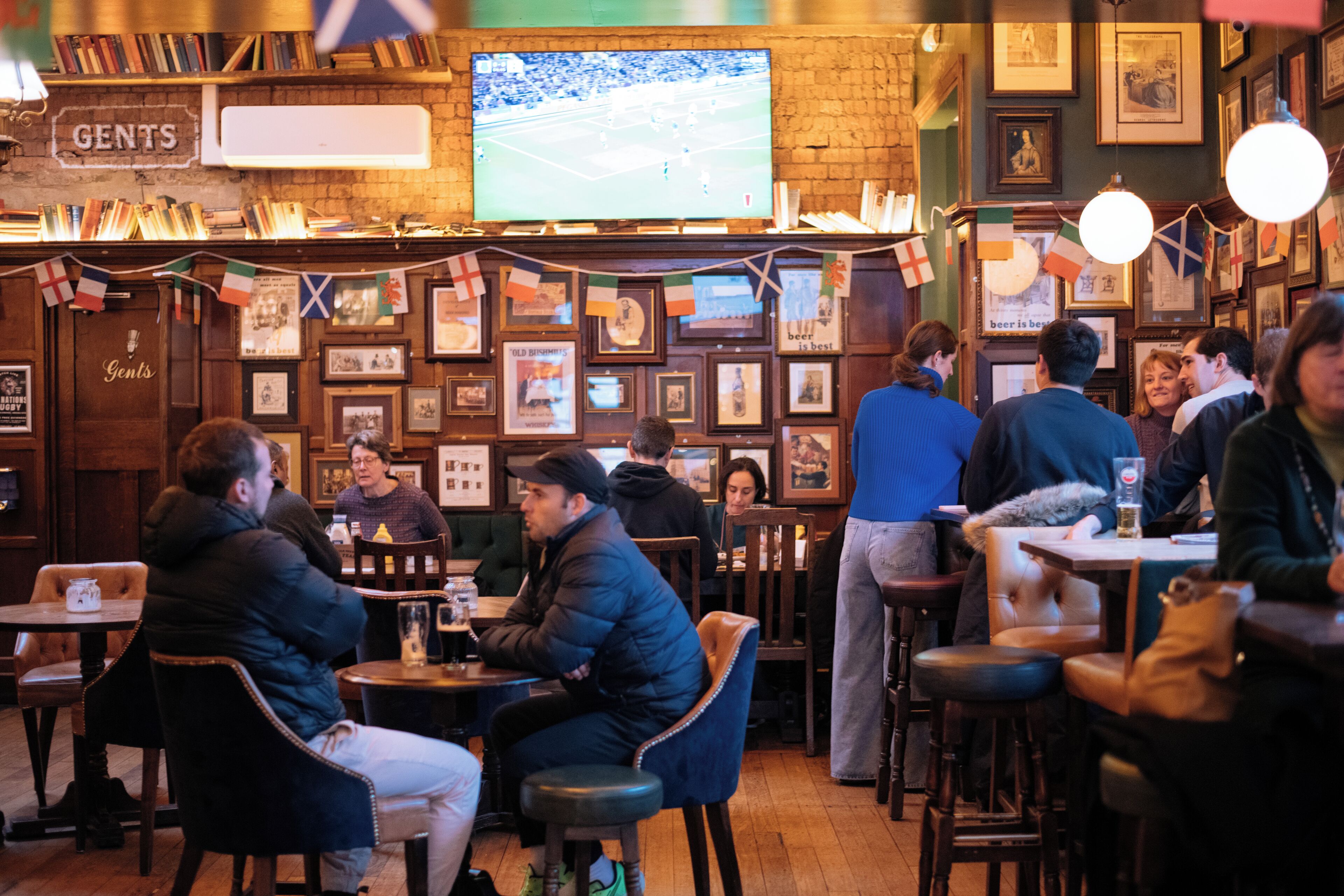 Um pub acolhedor com paredes de madeira, uma grande tela de televisão e várias bandeiras.