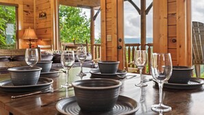 Uma cabana de madeira com uma mesa de jantar posta para quatro pessoas, com tigelas de cerâmica escura e taças de vinho.