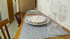 Uma área de refeições com uma mesa de madeira posta para dois, com jogos americanos estampados e louça decorada com flores.