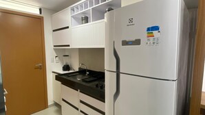 Uma cozinha compacta com armários brancos, bancada preta e geladeira branca.