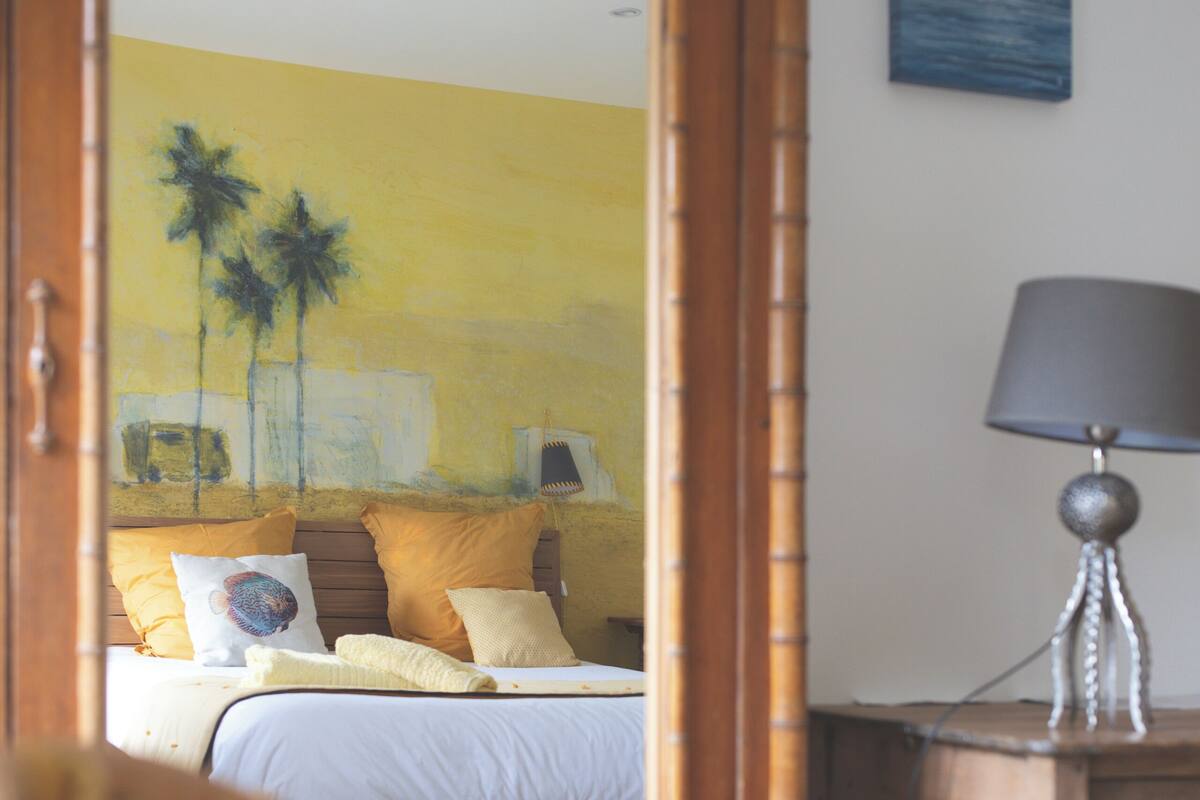Quarto com cama, mesa de cabeceira de madeira, abajur e quadro na parede.