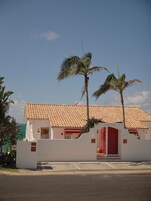 Um edifício com telhado telhado, porta vermelha e palmeiras à frente.