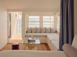 Uma sala de estar com sofá, mesa de centro de vidro e vista para o mar através de grandes janelas.