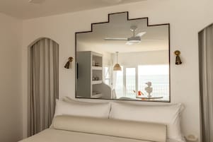 Quarto de hotel com uma cama grande, um guarda-roupa, um espelho e vista para o mar.