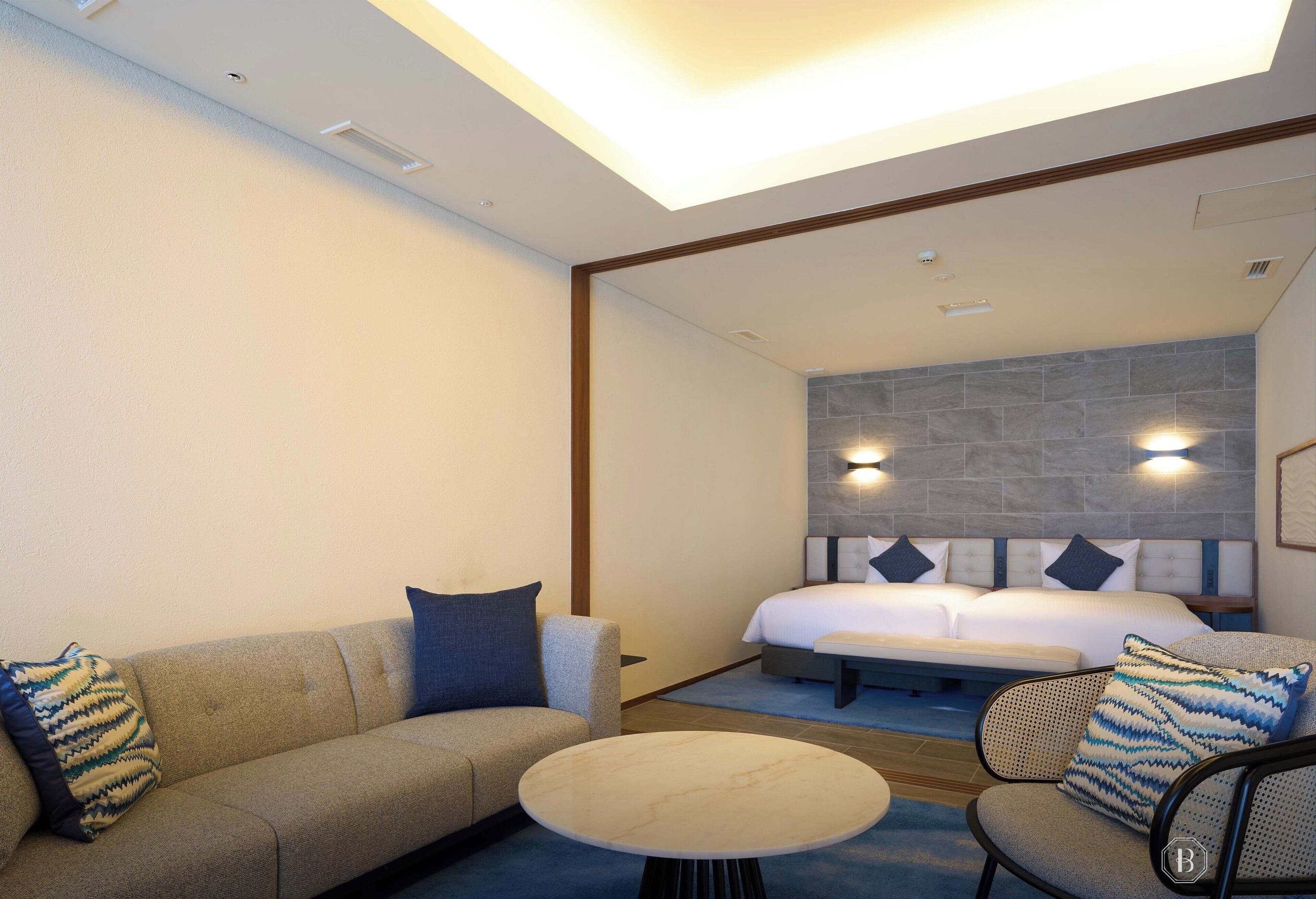 Quarto de hotel moderno com sofá, mesa de centro redonda e cama com cabeceira.