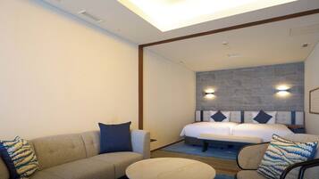 Quarto de hotel moderno com sofá, mesa de centro redonda e cama com cabeceira.