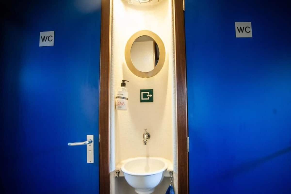 Um banheiro com porta azul, pia branca, espelho e vaso sanitário.