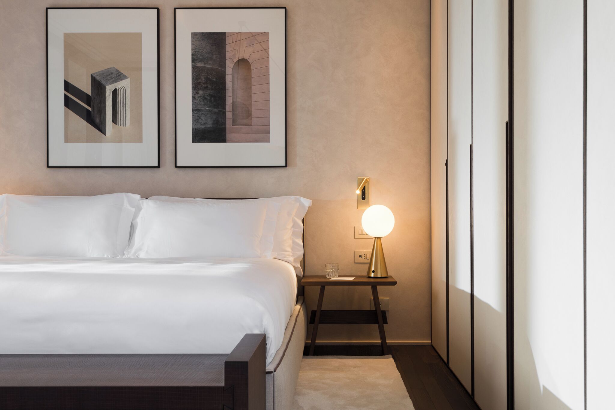 Quarto bem arrumado com cama, mesa de cabeceira e duas fotografias emolduradas na parede.