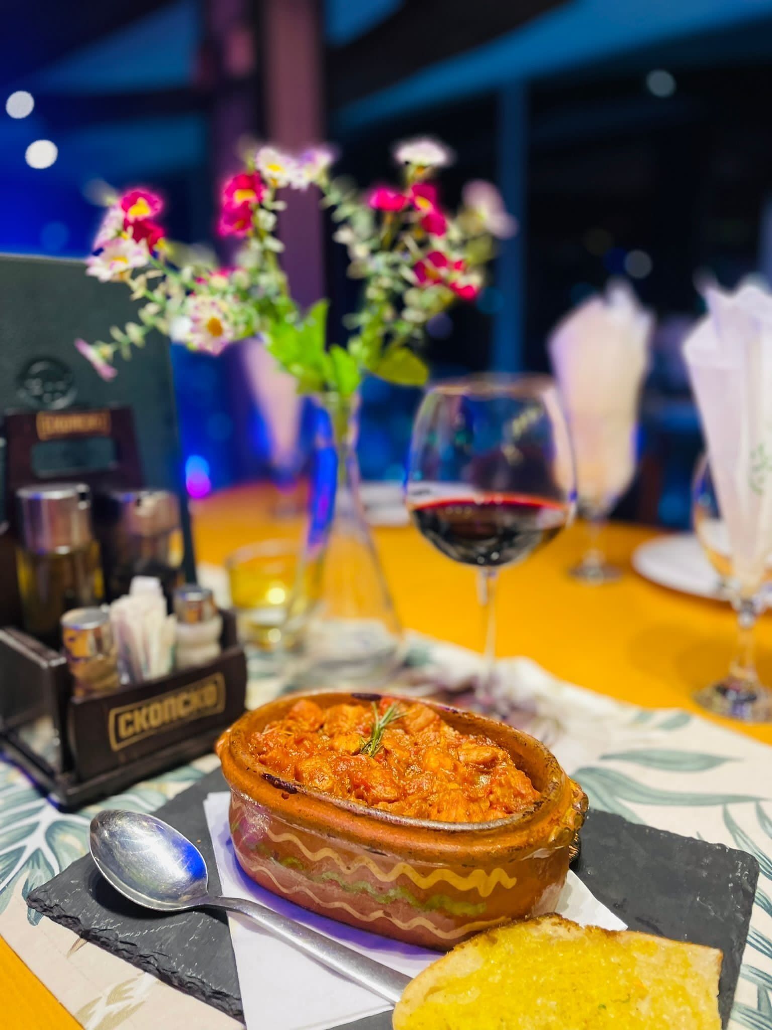 Uma mesa de jantar com um prato de comida, um copo de vinho tinto e um vaso de flores.