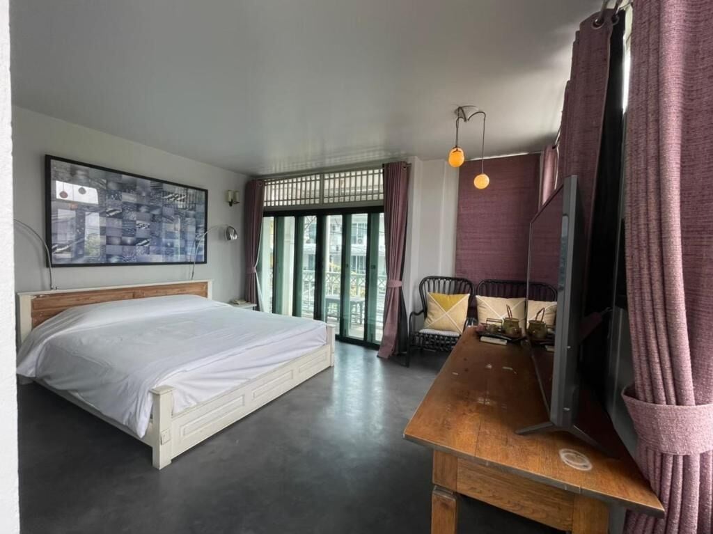 Quarto com cama, mesa de madeira, cadeira e vista para o exterior através de uma janela.