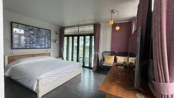 Quarto com cama, mesa de madeira, cadeira e vista para o exterior através de uma janela.