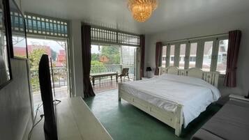 Quarto com uma cama grande, televisão e varanda com vista para edifícios.