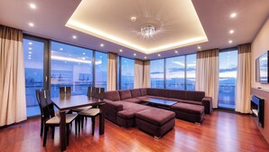Uma sala de estar moderna com um sofá seccional, uma mesa de jantar com cadeiras e grandes janelas com vista para a cidade.