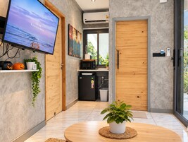 Um interior moderno com uma TV de tela plana exibindo uma paisagem, uma área de cozinha com micro-ondas e uma mesa de jantar com planta em vaso.