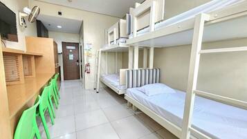Quarto de dormitório com beliches, escrivaninha, cadeiras e extintor de incêndio.