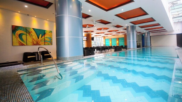 Uma piscina interior com piso em padrão Chevron, um grande pilar cilíndrico e uma pintura abstrata colorida na parede.