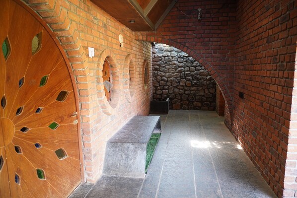 Um corredor com paredes de tijolo, um arco de pedra e uma porta de madeira com padrão geométrico.