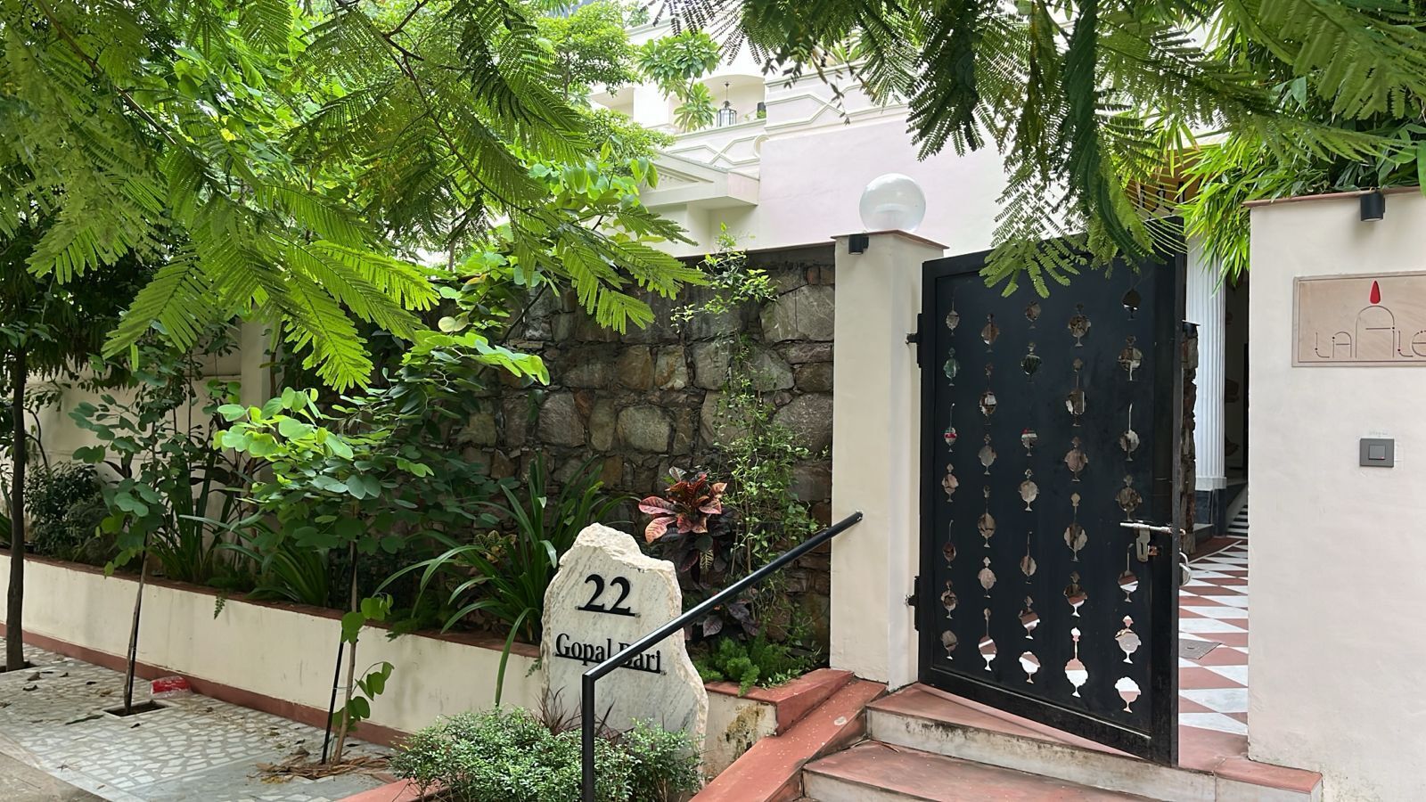Placa de pedra com o número 22, um portão decorativo preto e uma escadaria que leva a um edifício branco.