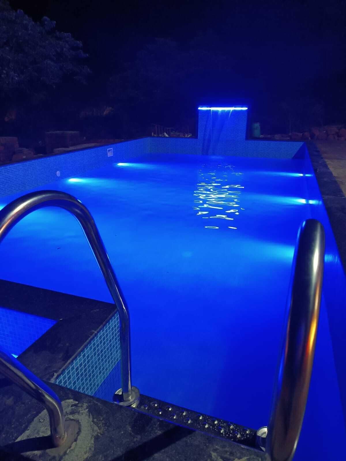 Uma piscina com um recurso aquático iluminado em azul e uma escada de metal dando acesso à água.