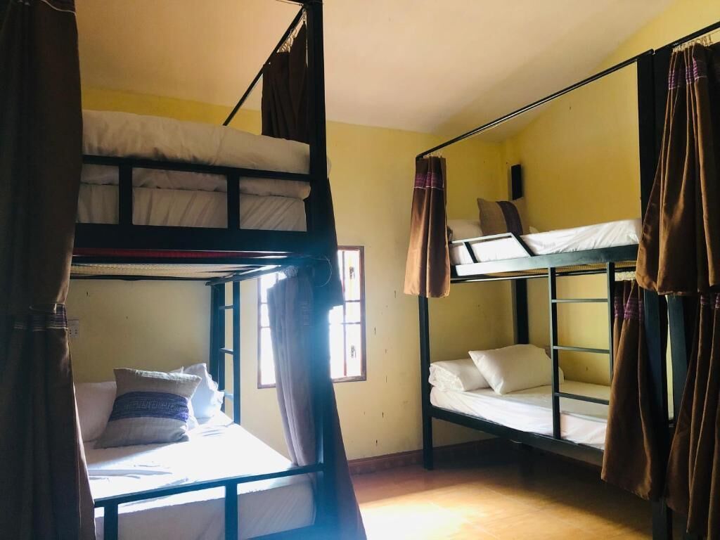 Um dormitório com beliches, cortinas e uma janela.