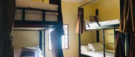 Um dormitório com beliches, cortinas e uma janela.