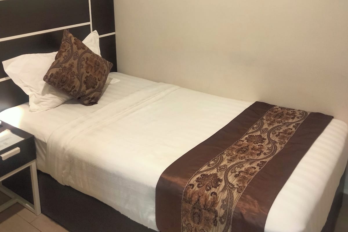 Uma cama bem arrumada com um manta estampada, um travesseiro e uma mesa de cabeceira com uma luminária.