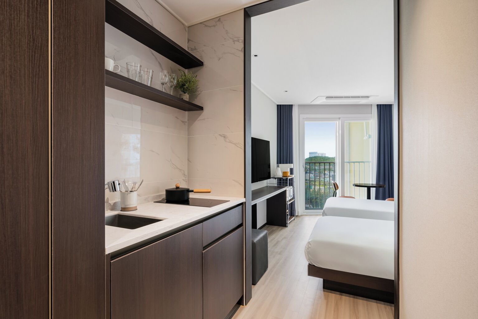 Quarto de hotel moderno com cozinha, cama e varanda com vista para a cidade.