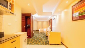 Quarto de hotel com cama, uma pequena escrivaninha, poltrona, sofá e cozinha equipada com frigorífico e armários.