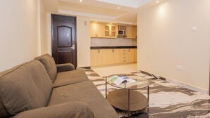 Sala de estar com sofá e mesa de centro, cozinha ao fundo e uma porta que dá para outro cômodo.