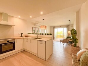 Cozinha moderna com ilha central, área de refeições com planta de cacto e vista para o exterior.