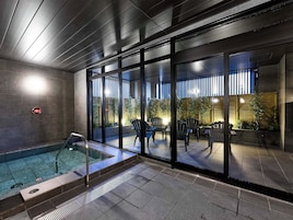 Área interna de piscina com paredes de vidro, um relógio digital e um espaço de estar com cadeiras.