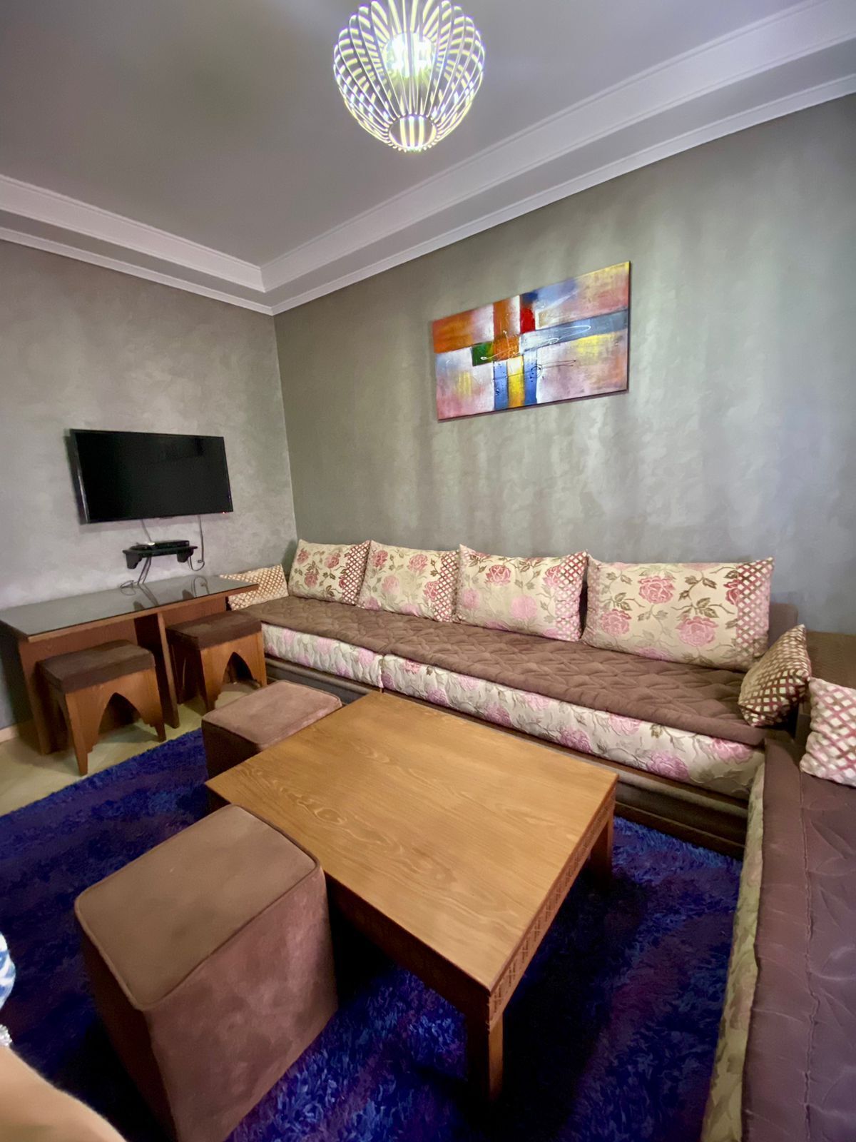 Uma sala de estar com sofá, mesa de centro, televisão e um quadro na parede.