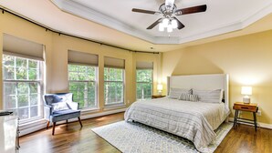 Quarto com uma cama grande, uma cadeira, ventoinha no teto e várias janelas.
