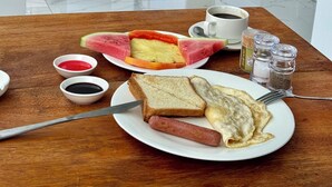 Uma mesa de café da manhã com torradas, um cachorro-quente, um prato de frutas, café, acompanhamentos e uma faca.