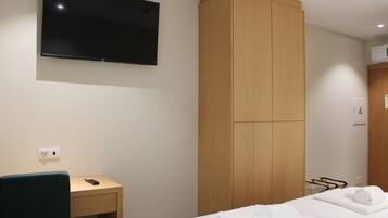 Quarto de hotel com uma cama, uma escrivaninha, televisão e guarda-roupa.