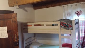 Uma cama beliche com teto de madeira, uma porta com um papel fixado e uma janela com cortinas em formato de coração.