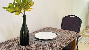 Uma mesa de jantar com toalha de mesa estampada, um prato branco, talheres e uma planta verde num vaso.
