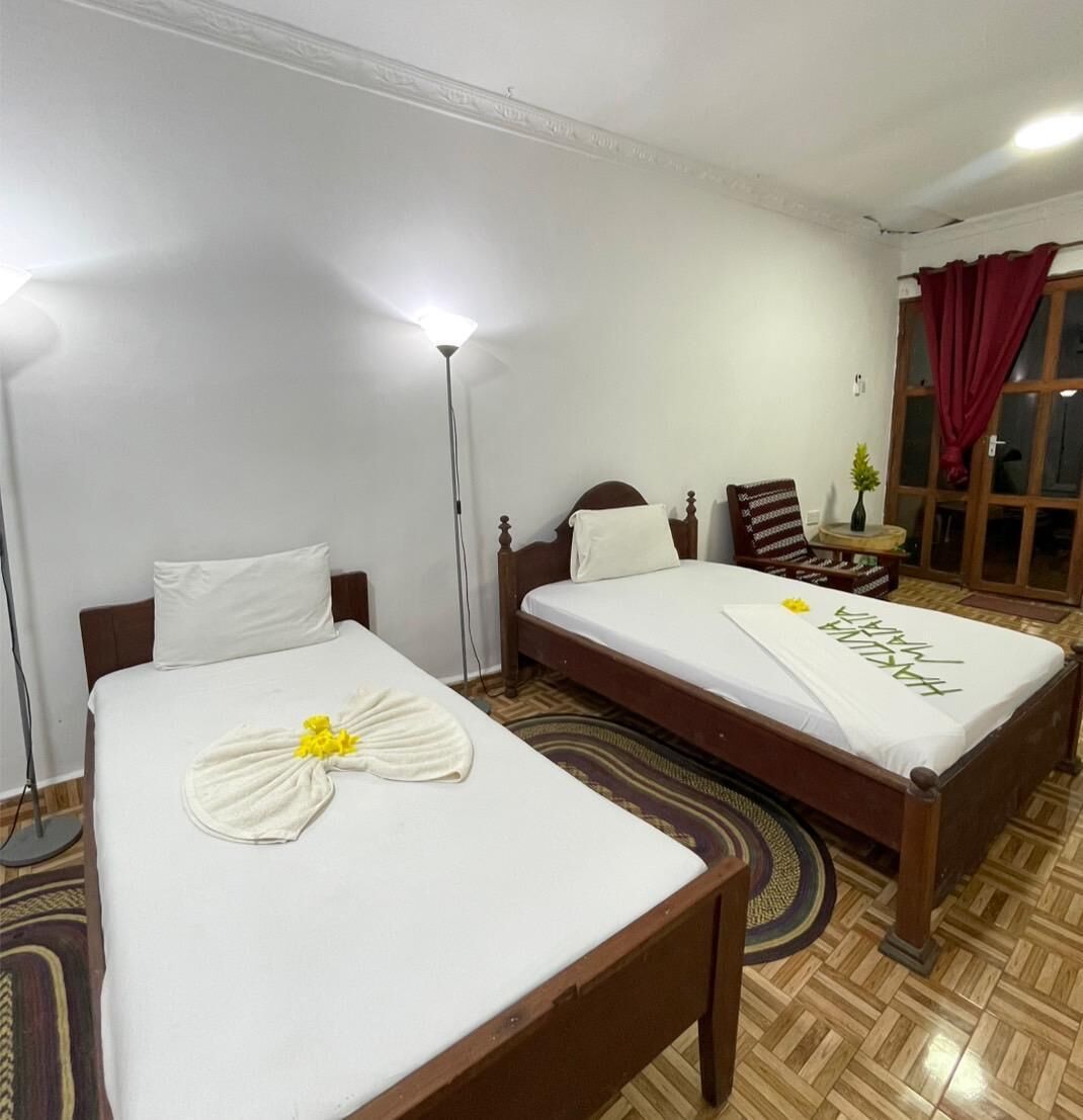 Quarto de hotel com duas camas de madeira, roupa de cama branca e uma mesa pequena com um vaso.