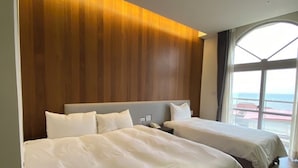 Quarto de hotel com duas camas, cabeceira de madeira e uma janela grande com vista.
