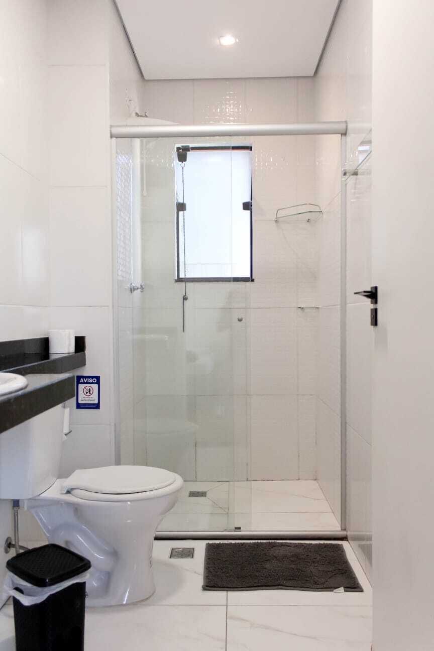 Casa de banho moderna com chuveiro em cabine de vidro, sanita branca e um lixo preto.