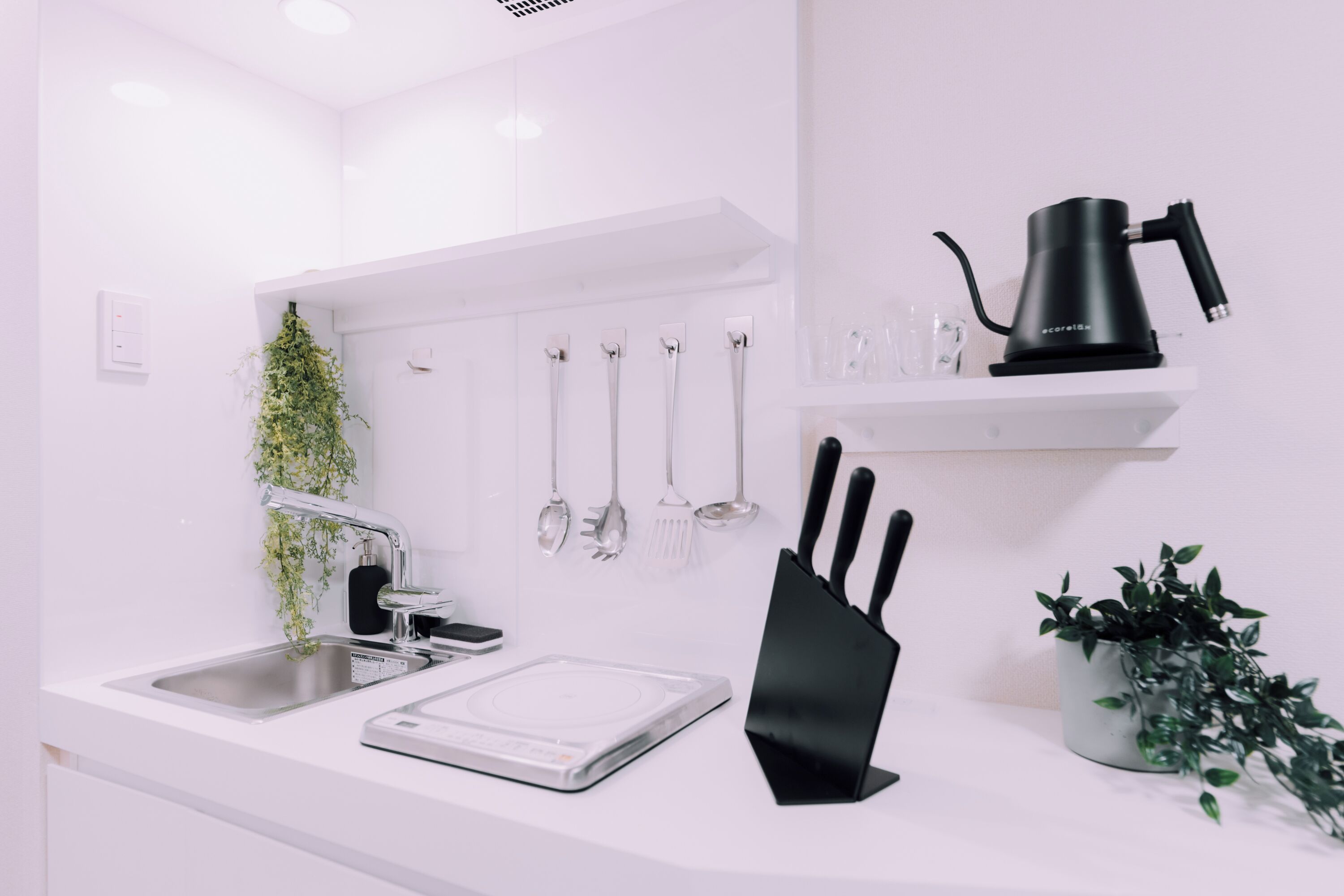 Cozinha moderna com bancada branca, pia de aço inoxidável e cafeteira preta em prateleira branca.